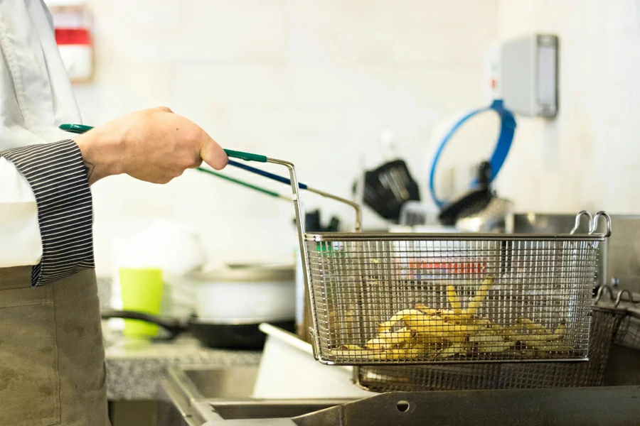 Cook preparing French fries in a kitchen.